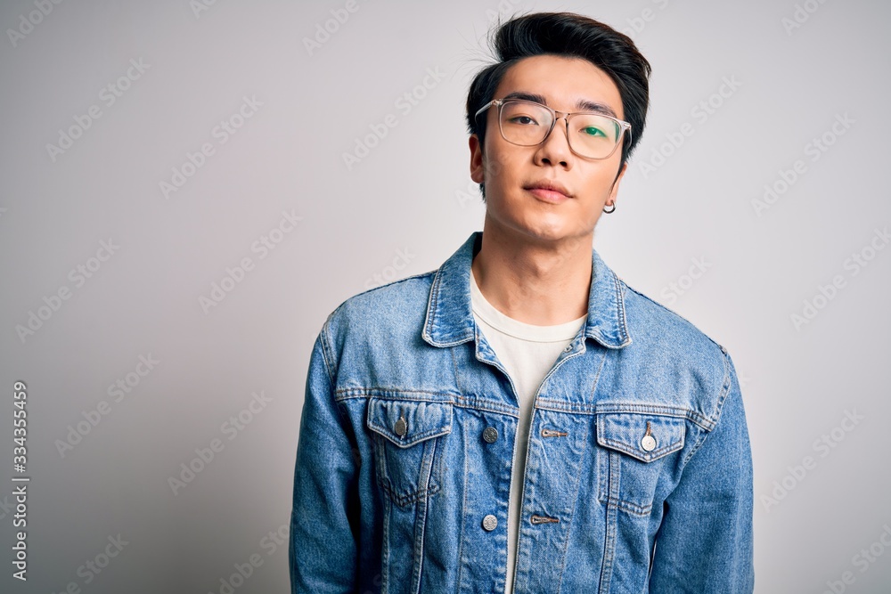 Young handsome chinese man wearing denim jacket and glasses over white ...
