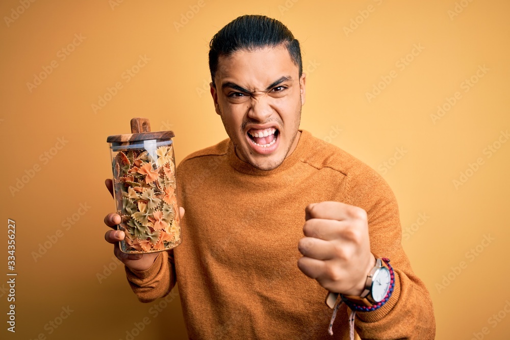 Young brazilian man holding jar with Italian dry pasta over isolated ...