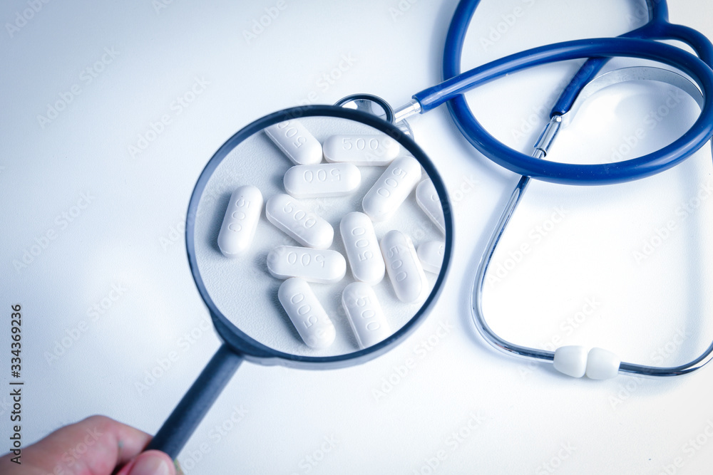 The doctor holds a magnifying glass to see the white pill to treat the ...