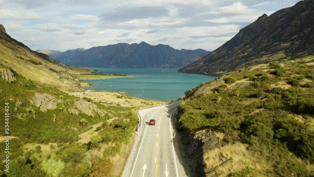Red Car Driving on Open Road towards Big Blue Lake with Mountains in ...