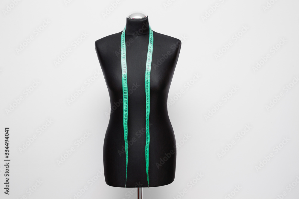 Black mannequin with green measuring tape at light gray wall background ...