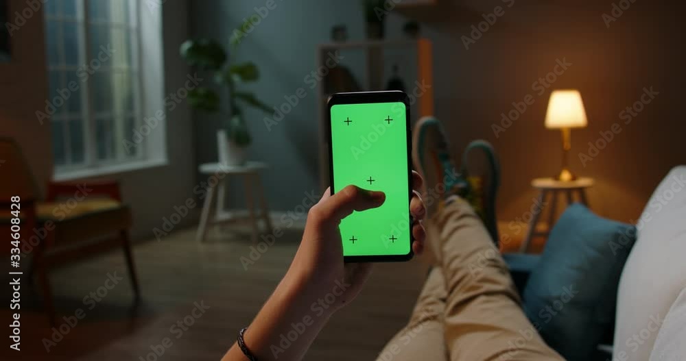 Man lying on couch using smartphone with chroma key green screen at night, scrdoing various ...