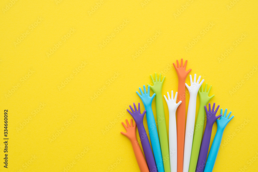 Many colorful hands up on yellow background with copy space. Concept of ...
