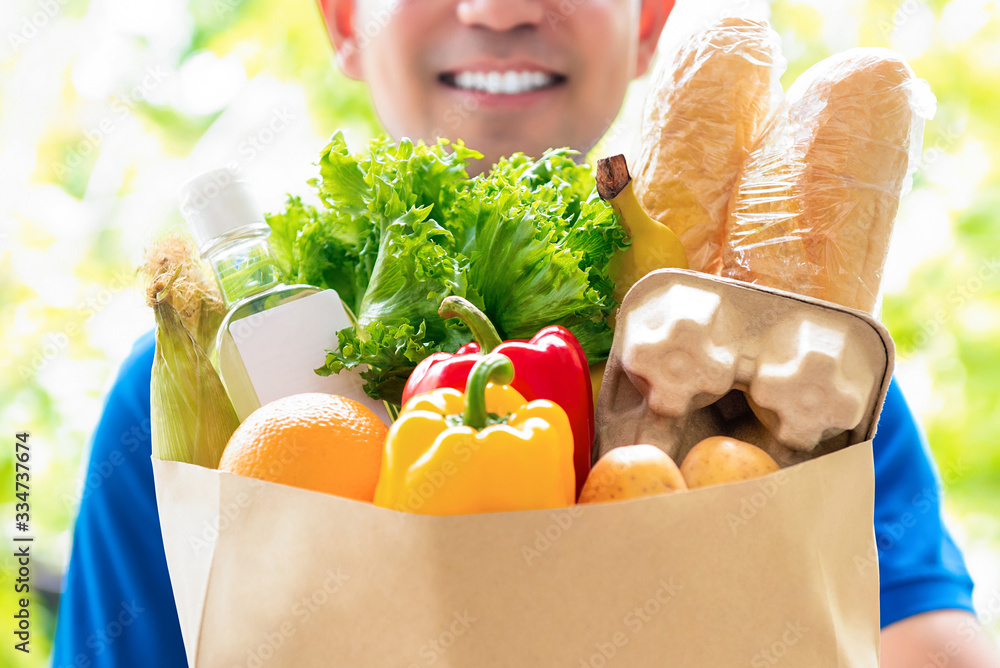 Smiling delivery man holding a grocery bag ready to deliver to the ...