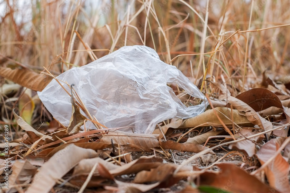 Garbage from plastic bags that are thrown away on the dry leaves ground ...