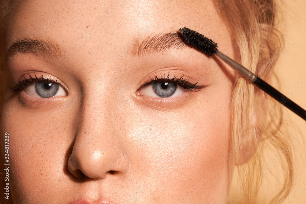 Close-up of a young girl brushing her eyebrows on her face. Fresh ...
