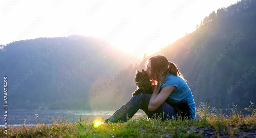 Young woman sitting on grass and petting cat Side view of young happy ...