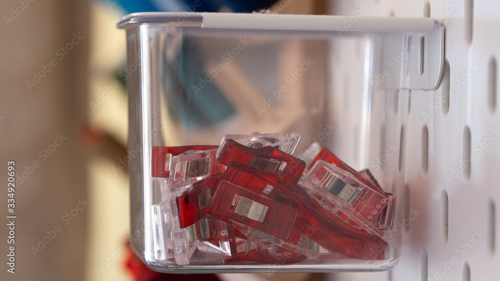 Close up on clips stored inside a clear box hanging from peg board as a ...