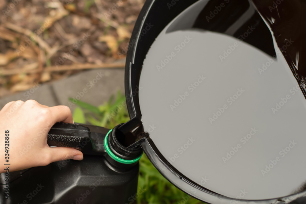 Transfering of used drained motor oil from the black tray to the empty ...