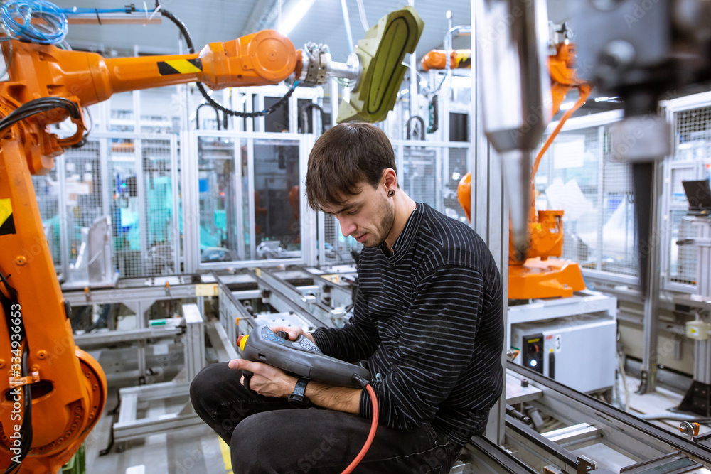 Programmer programming automatic robot arms in automotive smart factory ...