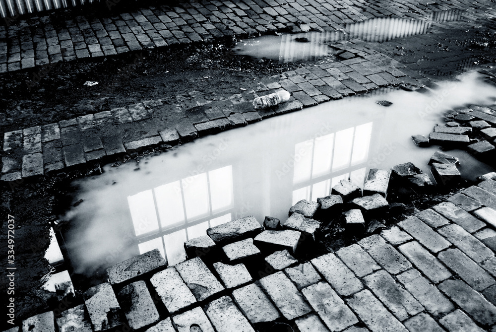 Windows in reflection of puddle on old pavement resembles a bottle ...