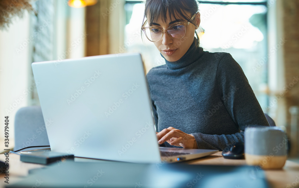 portrait of skilled young female developer in eyeglasses concentrating ...