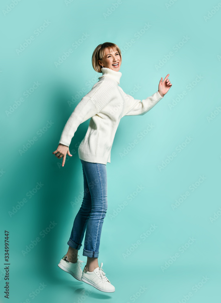 Blonde woman in white sweater, jeans and sneakers. She is laughing ...