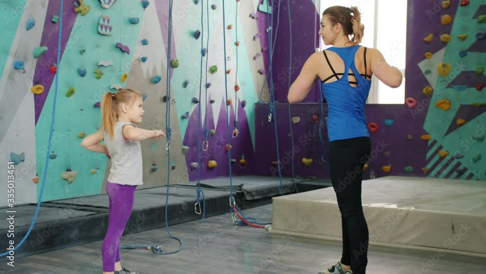 Little girl is exercising indoors in climbing gym with loving mother ...