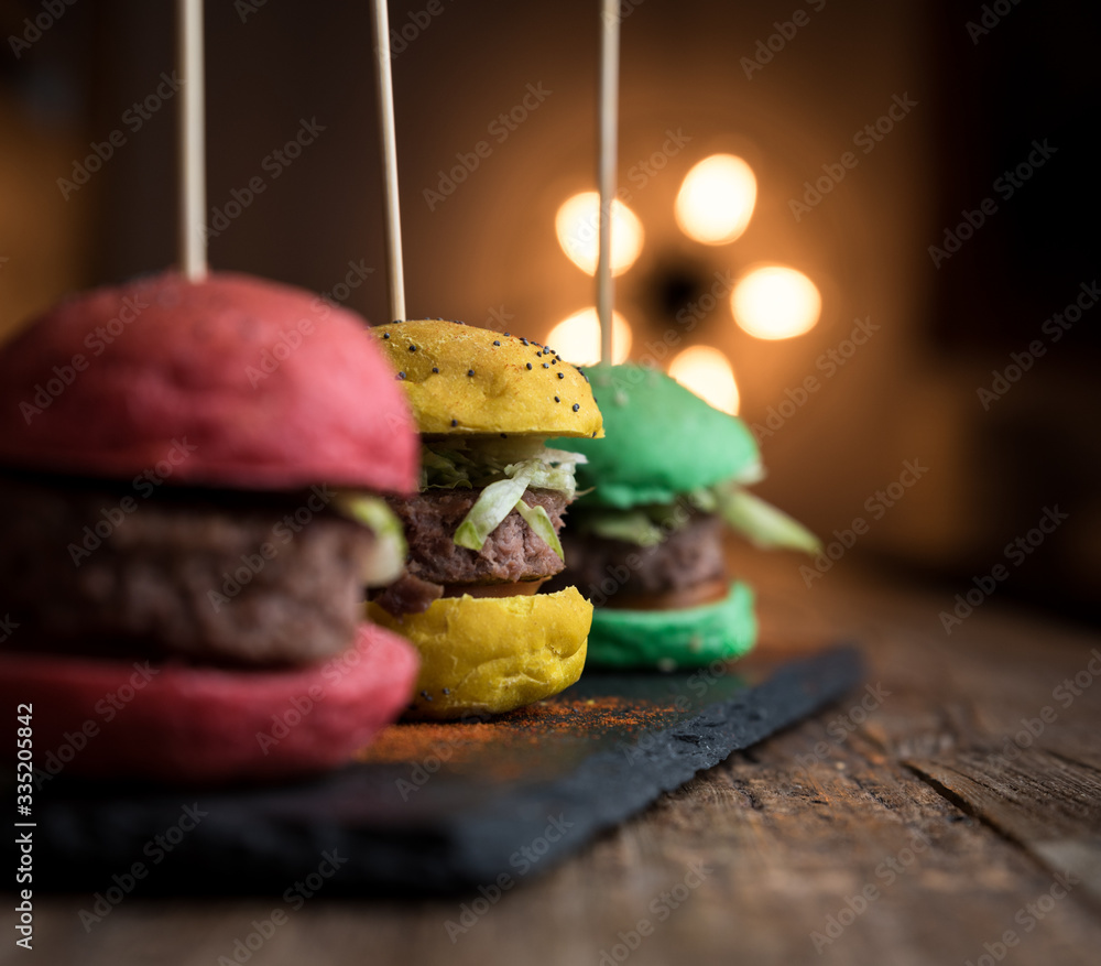 Mini hamburger colorati di manzo su piatto di ardesia, tavolo in legno ...