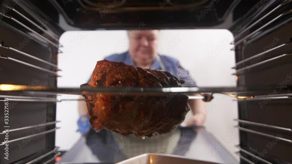 Woman cooking rotisserie spit roasted pork meat in oven at home ...