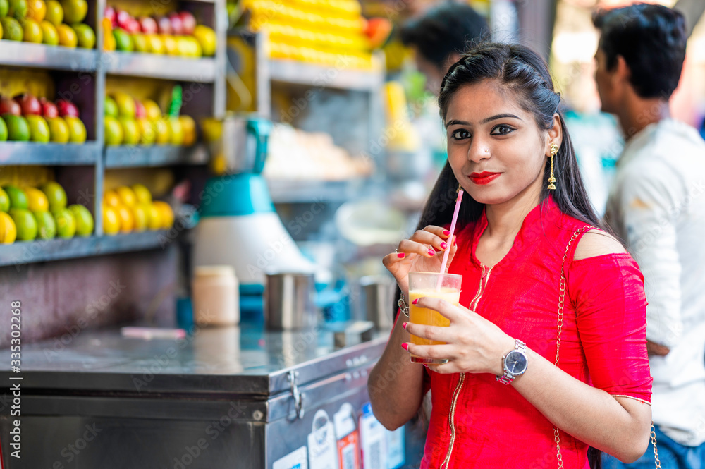 Young happy smiling Indian woman drinking orange juice outdoor in the ...