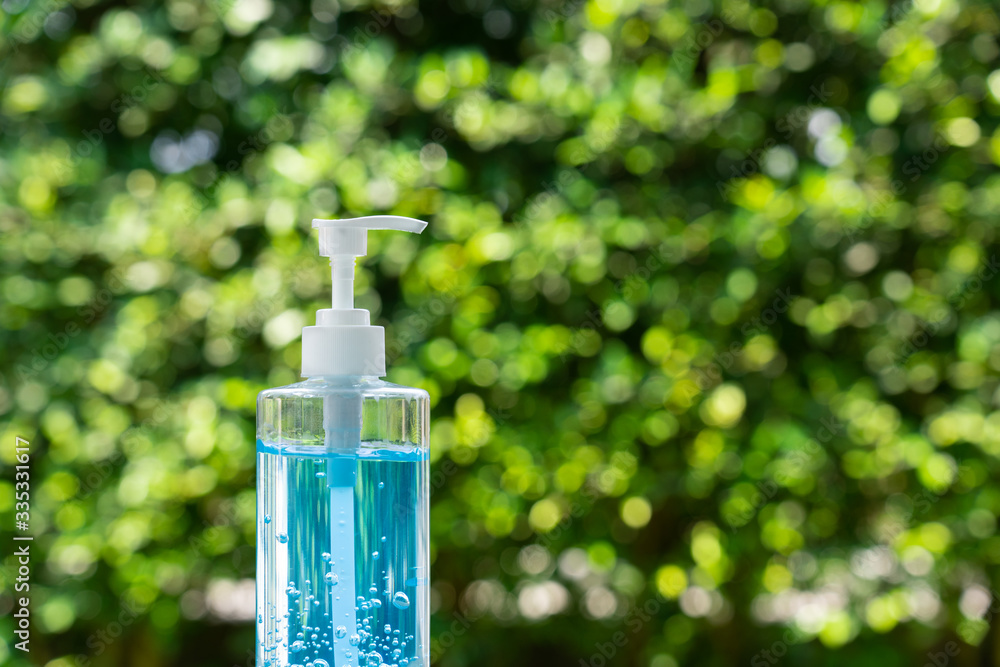 Blue hand sanitizer gel in clear pump bottle with green bokeh ...