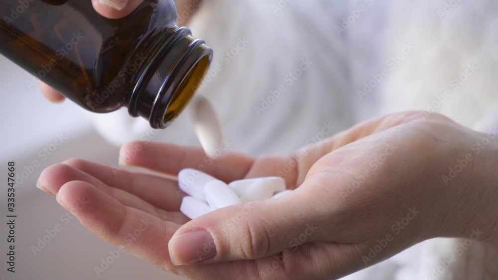 Woman pouring pills from bottle into palm. Close-up of pills in hand ...