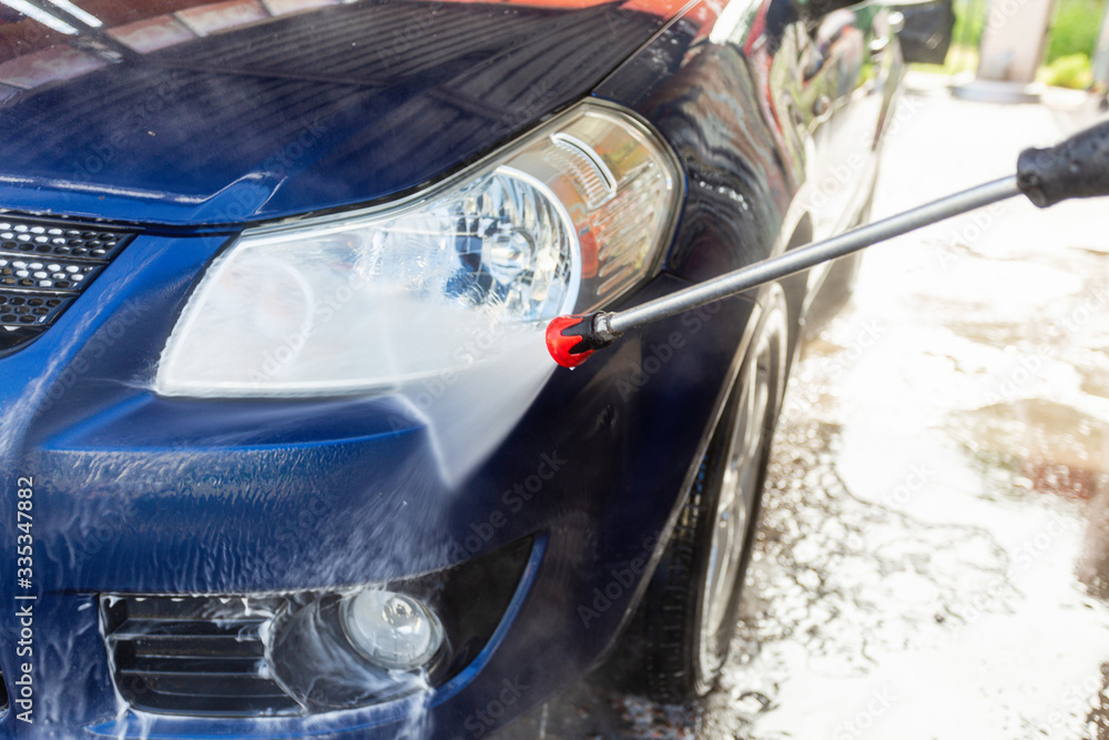 Close-up man holding a high-pressure water sprayer for car front lights ...