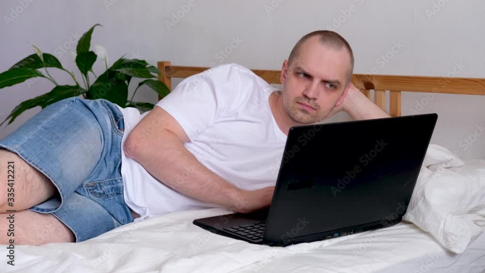 4k Man working office work remotely from home on bed. Using computer ...