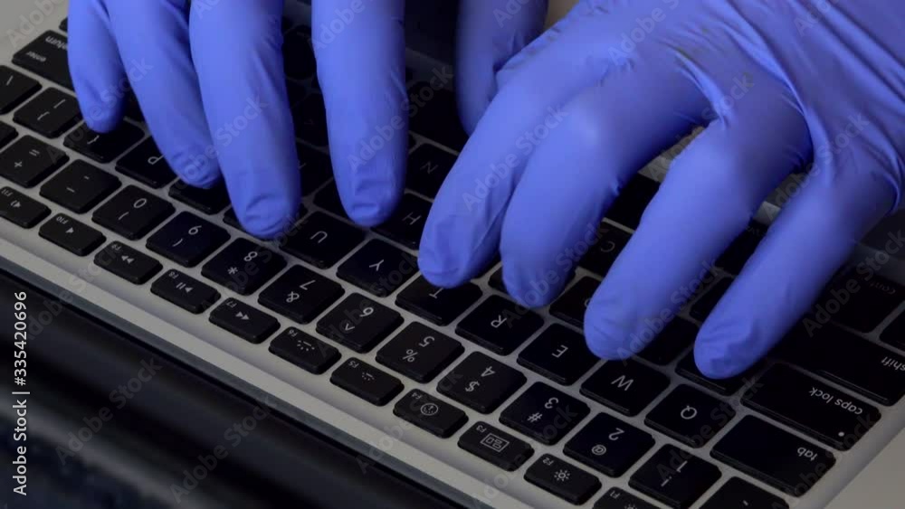 Hands wearing blue nitrile rubber gloves are shown typing on a laptop ...