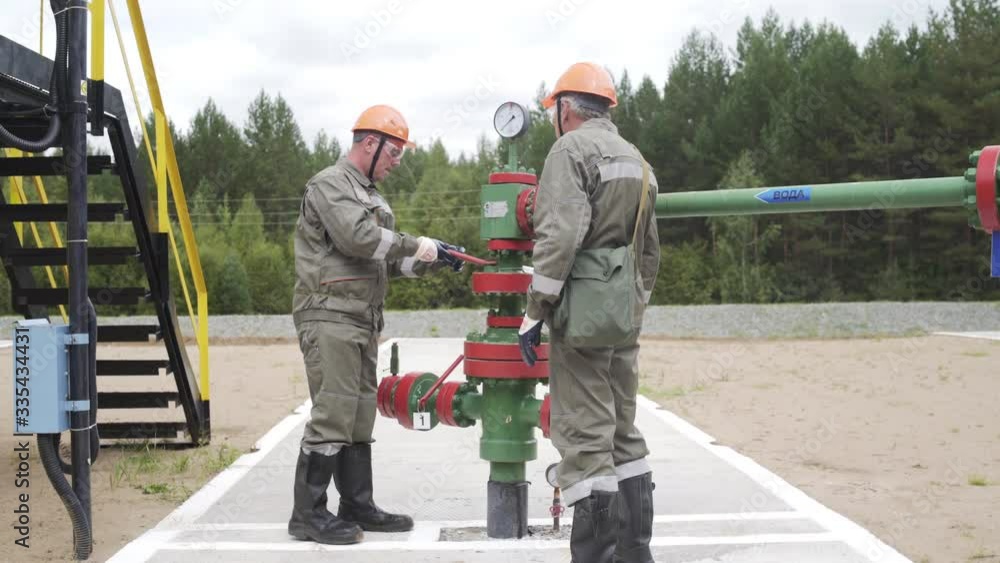 Oil field technical workers opening or closing valve of wellhead ...