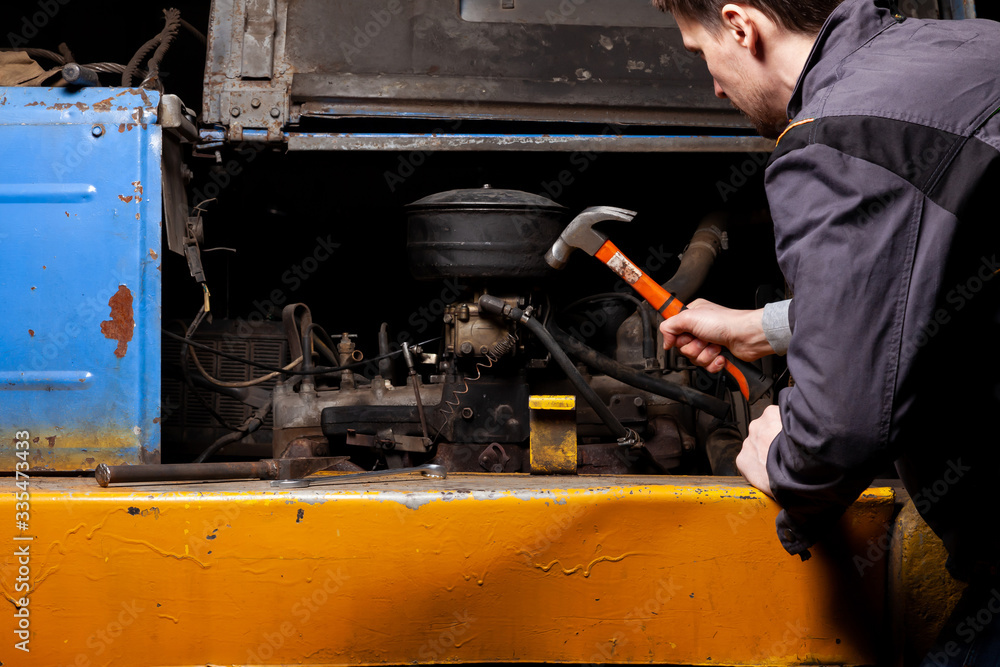 An angry male mechanic is repairing the engine of an old truck with an ...