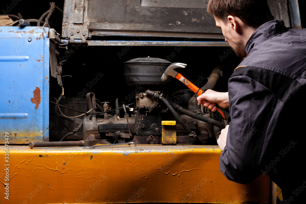 An angry male mechanic is repairing the engine of an old truck with an ...