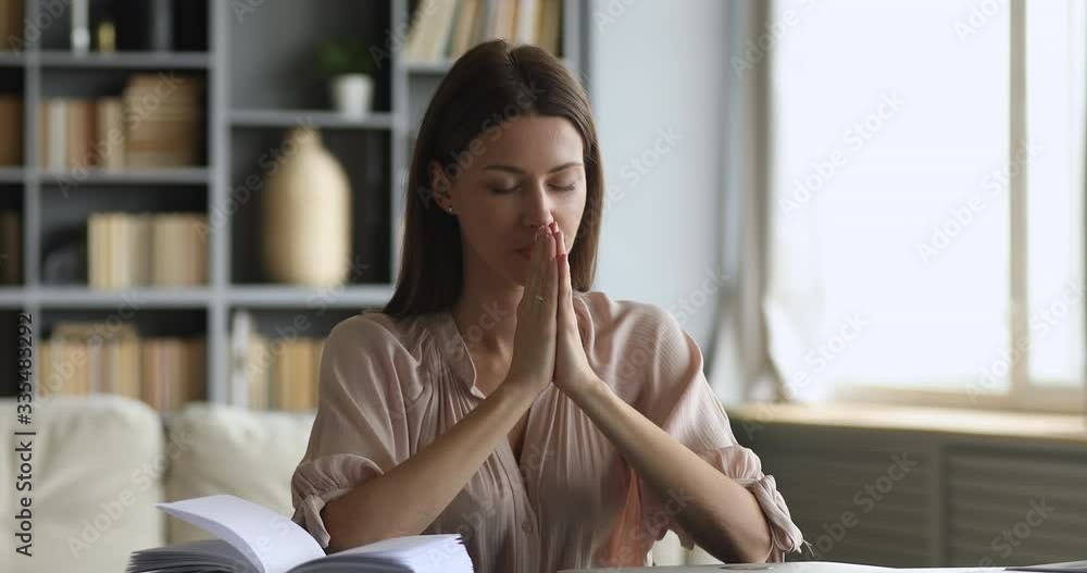 Young faithful mindful woman sitting at table with folded namaste hands ...