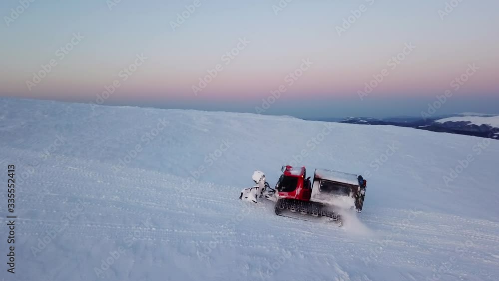 Snowcat rises uphill at dawn, aerial shoot. Climbing a snowcat on a ...