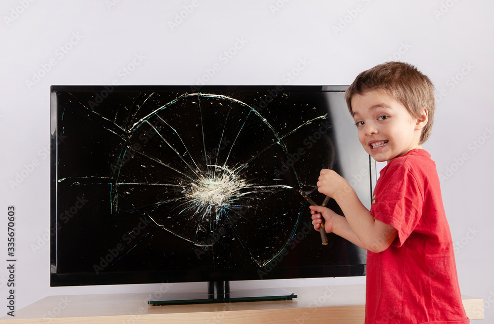 Cute little boy standing in front of a TV with broken screen holding a ...