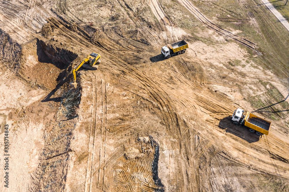 top down view of an excavator and dump trucks working on construction ...