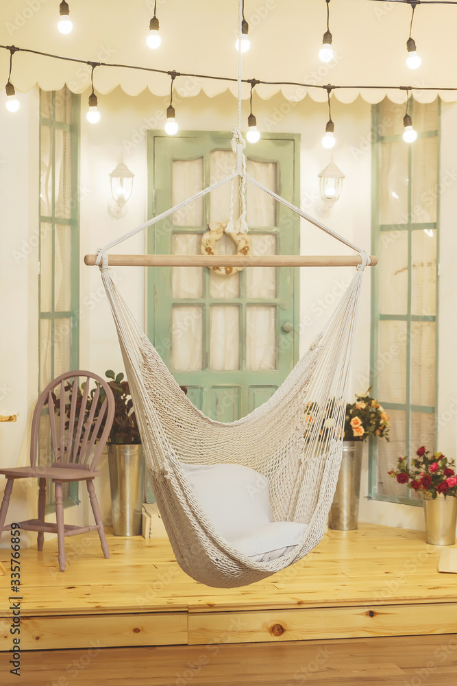 Suspended wicker swing on the summer porch with garlands of light bulbs ...