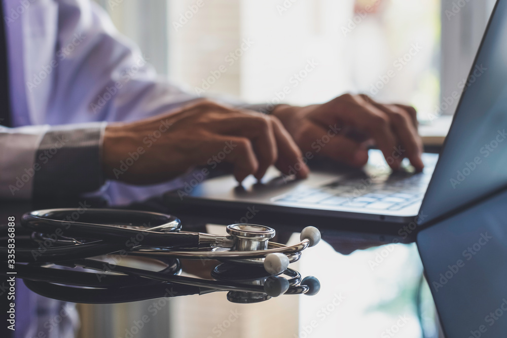 Male doctor in white coat typing on laptop computer keyboard with ...