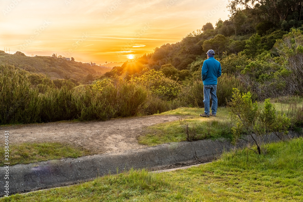 Man standing, watching the sunrise over hills and valley with trees and ...