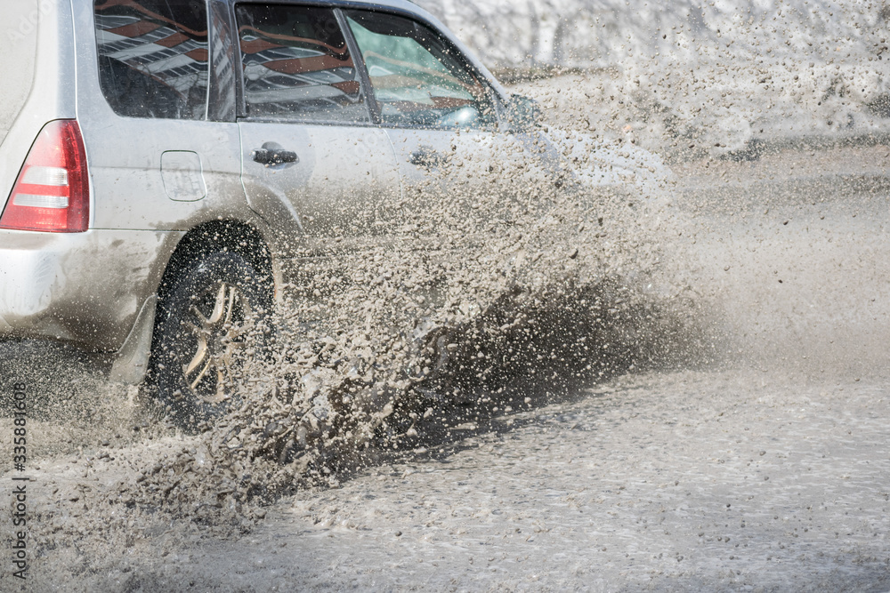 Car motion through big puddle of water splashes from the wheels on the ...