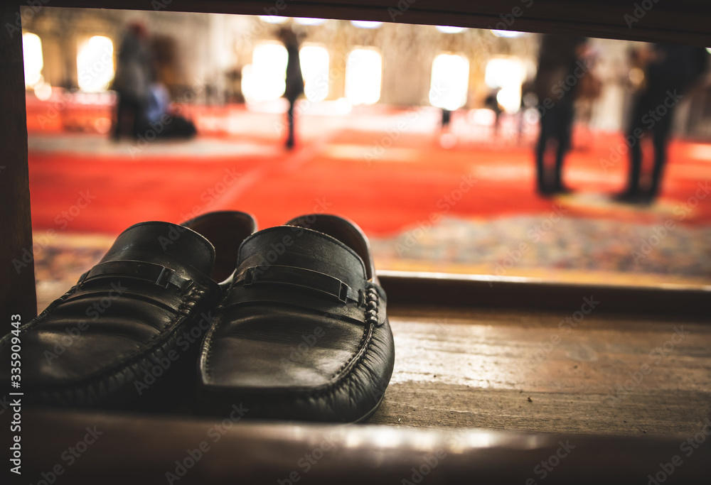 Black shoes on the shelf in a mosque with muslim people walking and ...