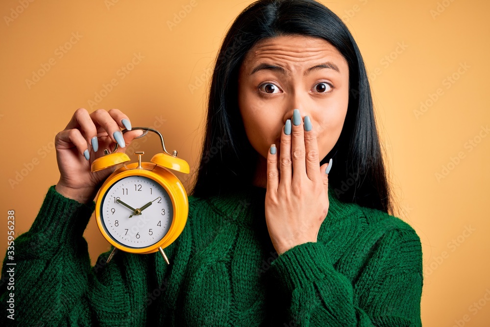Young beautiful chinese woman holding vintage alarm clock over isolated ...