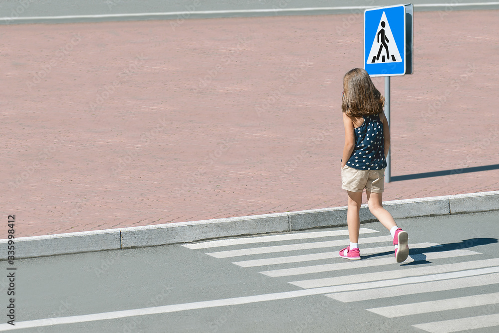 Stylish child in fashion clothes is walking along summer city crosswalk ...