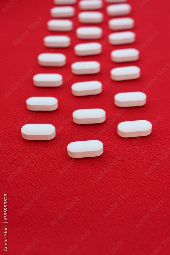 Medicine concept. White tablets are laid out in a line on a red ...