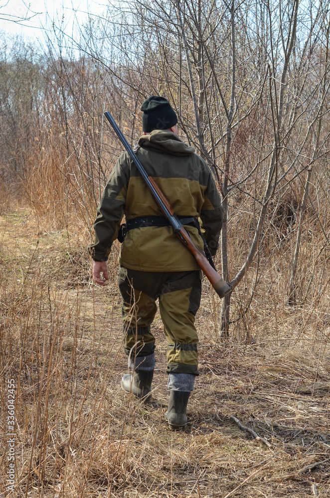 The hunter goes through the forest with a rifle on his back rear view ...