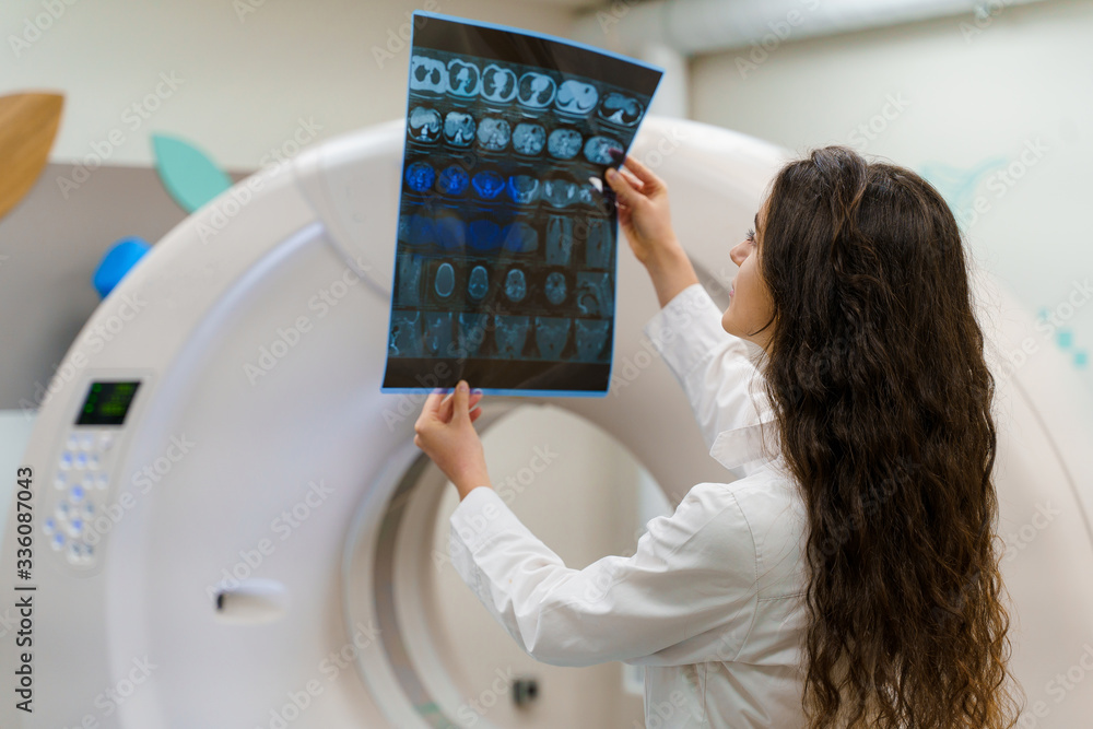 Young caucasian girl doctor looks at x-ray picture of patient brain ...