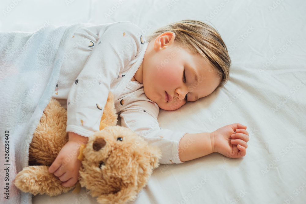 Toddler baby sleeping on white sheets hugging soft brown teddy bear ...