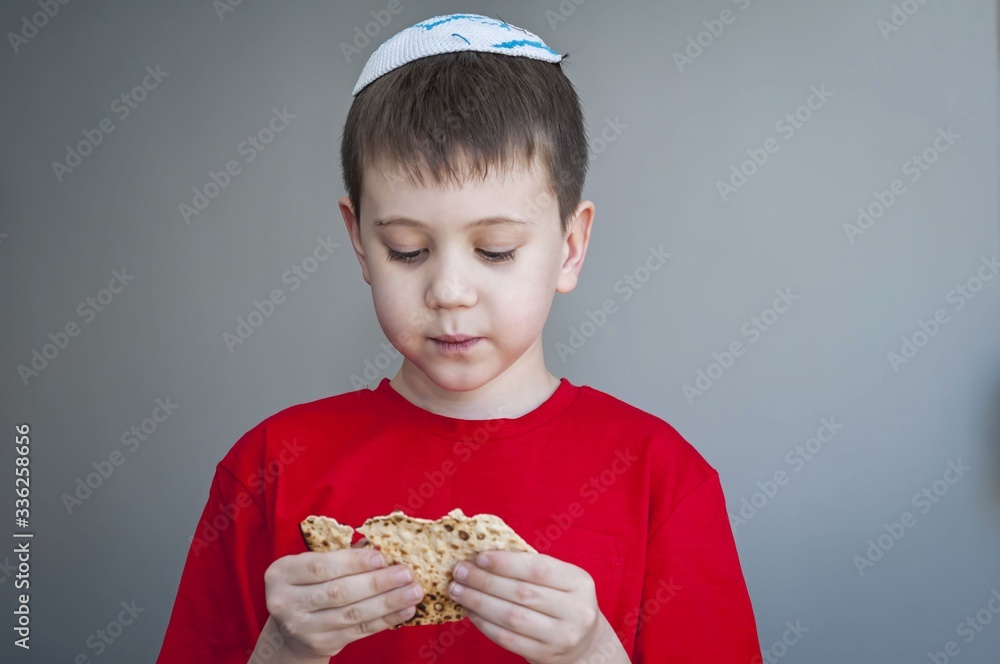 Cute Caucasian child in a white kippah cap eating shmura matzo, a piece ...