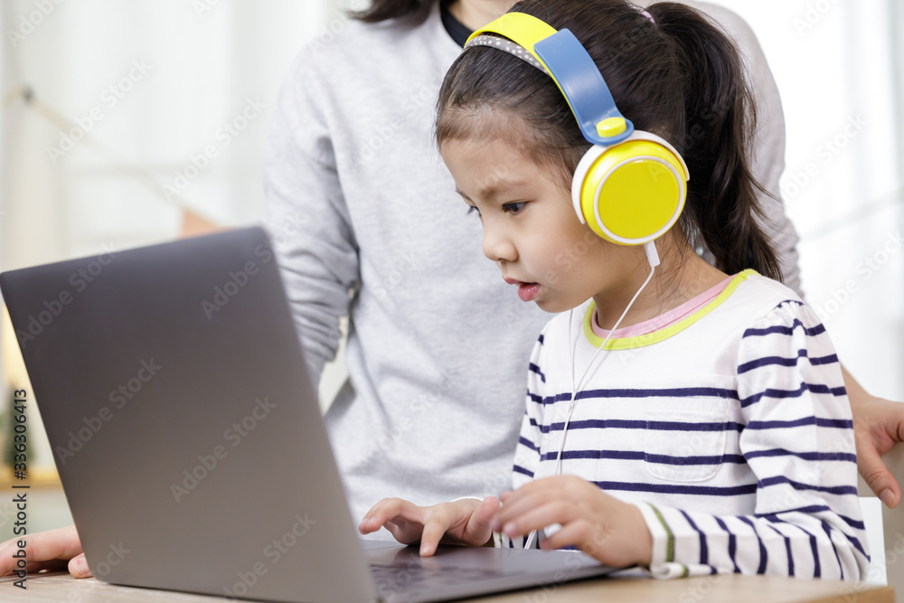 Asian little child girl learning at home with laptop computer using ...
