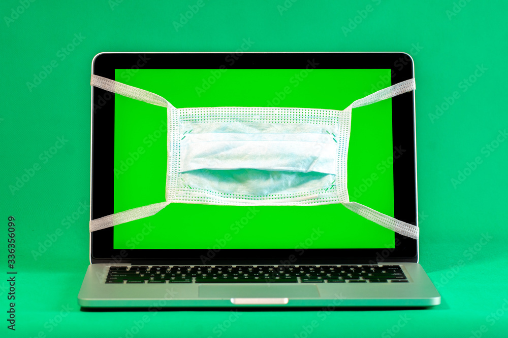 An open laptop with a sterile medical mask on a green screen is ...