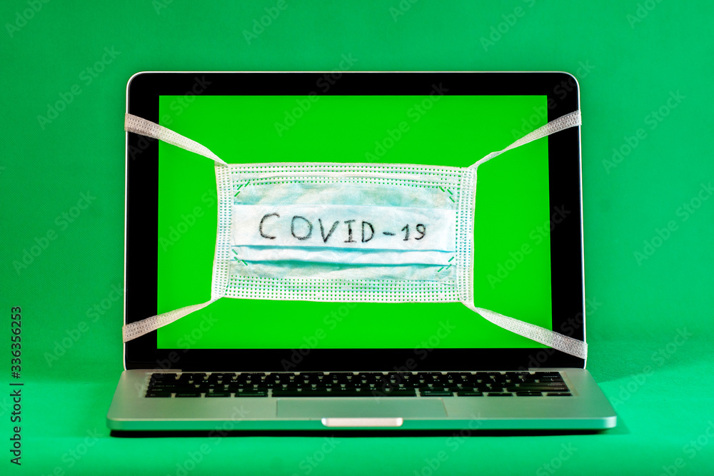 An open laptop with a black Covid-19 mask inscribed on a green screen ...
