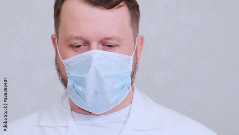 bearded male doctor takes off his protective mask with a sad look. This ...