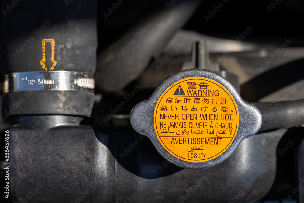 Orange radiator cap with warning labels in different languages: never ...